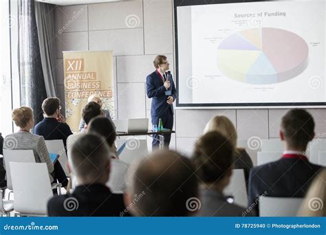 Businessman Explaining Pie Chart To Audience In Seminar Hall Stock