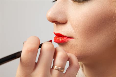 스튜디오에서 메이크업 아티스트는 그녀의 손에 붉은 색의 립스틱을 적용 하기 위한 브러시를 보유 하 고 있는 어린 소녀 금발에 고급 스러운 동양 메이크업을 부과 갈색에 대한