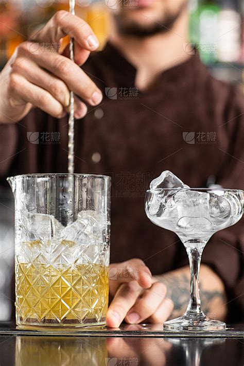 专业调酒师用勺子搅拌冰凉的鸡尾酒吧台上放着几瓶酒精饮料和玻璃杯