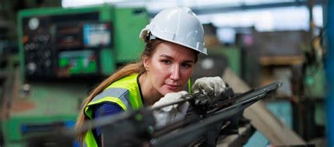 안전 하드 햇 헬멧을 착용 한 백인 여성 엔지니어링 근로자는 자동 로봇 선반 기계를 검사하여 부품을 드릴링합니다 금속 선반 산업