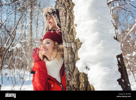 Playful Couple Hiding Behind A Tree Trunk In The Snow Stock Photo Alamy