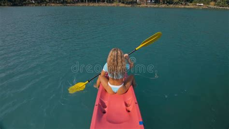 Seductive Blonde Woman In Blue Swimsuit Sails On Pink Plastic Kayak