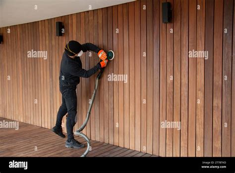 Deck Worker In Mask Sanding Hardwood Siding With Orbital Sander Wooden