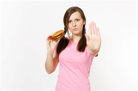 젊은 엄격한 여자 손바닥 중지 제스처를 보여주는 흰색 배경에 고립 손에 햄버거를 들고 적절 한 영양 섭취 또는 고전적인 미국의 패스트 푸드입니다 광고에 대 한 공간을 복사