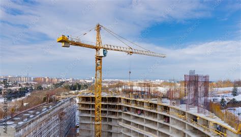 고층 건물 공사 현장에서 타워크레인이 자재를 올리고 있는 장면 ภาพถ่ายสต็อก Adobe Stock