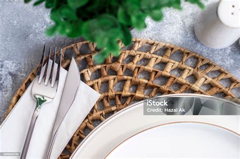하얀 도자기 접시와 나무 배경에 등나무 둥근 짠 플레이스매트 위에 은색 식기류가 있는 간단한 식탁 세팅 닫다 식기류에 대한 스톡 사진 및 기타 이미지 Istock
