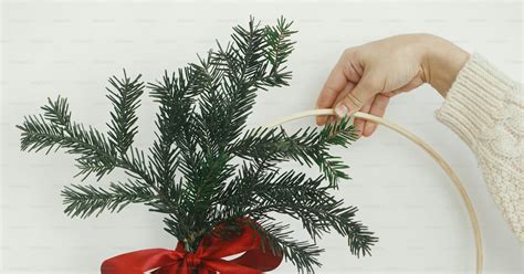 흰 벽 배경에 현대 크리스마스 화환을 들고 아늑한 스웨터를 입고 있다 메리 크리스마스와 해피 홀리데이 전나무 가지와 빨간 활을 손에 들고 있는 세련된 미니멀리즘