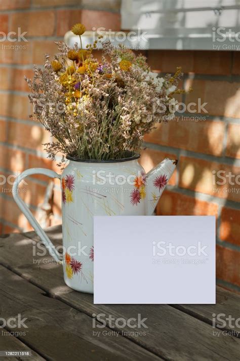 엽서 모형에 오래 된 에나멜 용기와 말린 꽃 텍스트 인쇄 또는 글자를 위한 공간이 있는 빈 카드입니다 빈티지 나무 테이블과 벽돌 벽 대기 순간 고대 유물에 대한 스톡 사진