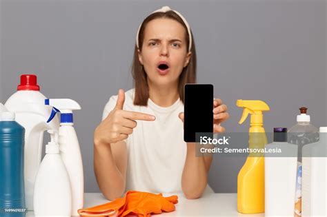 충격을 받고 놀란 놀란 여자는 회색 배경 위에 격리된 청소 세제를 들고 직장에서 포즈를 취하며 광고를 위한 빈 공간을 가리켰다 30 34세에 대한 스톡 사진 및 기타 이미지