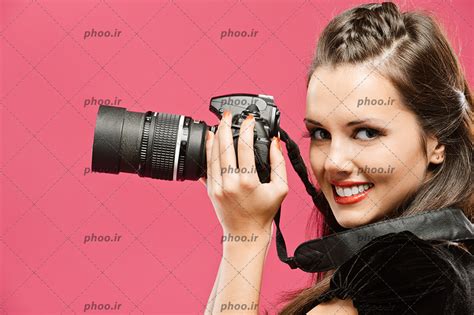 عکس با کیفیت دختر جوان زیبا با دوربین عکاسی حرفه ای در دست در پس زمینه صورتی عکس با کیفیت و