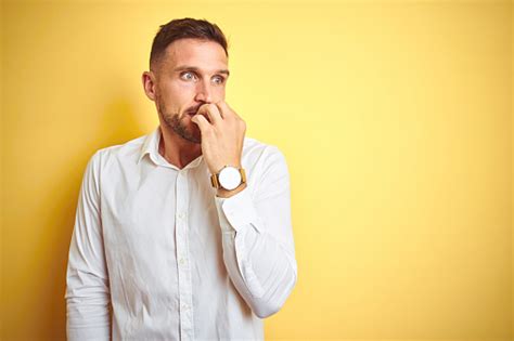노란색 고립 된 배경 위에 우아한 흰색 셔츠를 입고 젊은 잘 생긴 남자는 손톱을 물고 입에 손을 긴장 찾고 불안 문제 남자에 대한 스톡 사진 및 기타 이미지 Istock