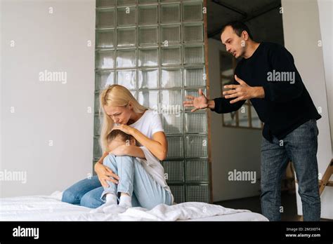 Portrait Of Scared Mother And Daughter Hugging Each Other While Father Angrily Yells At Them