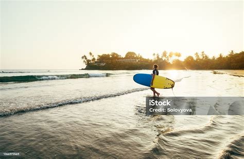 야자수 숲에서 일몰 광선으로 서핑을 위해 파도에 들어가는 파란색과 노란색 서핑 보드를 가진 십대 소년 행복한 어린 시절과 활동적인 스포티 한 사람들은 휴가 시간 개념 10