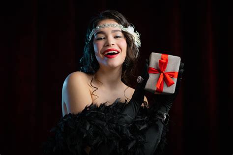 아르 데코 스타일의 옷을 입은 즐거운 빈티지 여성은 벨루어 배경에 활과 선물 상자를 들고 그녀는 선물을 기쁘게 생각합니다 복고풍 파티 패션 컨셉 고풍스런에 대한 스톡 사진