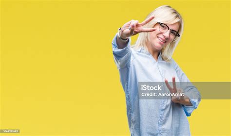 젊은 아름 다운 금발 비즈니스 여자 승리 표시를 하 고 손가락을 보여주는 카메라를 보고 웃 고 고립 된 배경 위에 안경 착용 번호 2입니다 여자 사업가에 대한 스톡 사진 및