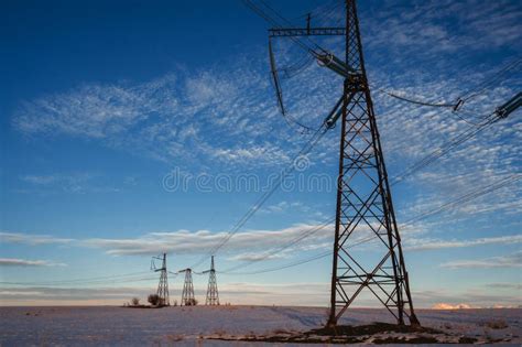 High Voltage Power Transmission Line With Towers In Field In Winter At Sunset In The Evening
