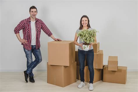 행복한 젊은 부부는 새 아파트로 이사했습니다 손에 화분과 여자와 그의 손으로 Akimbo와 남자는 카메라를보고있다 Grinnig 매우 행복 2명에 대한 스톡 사진 및 기타