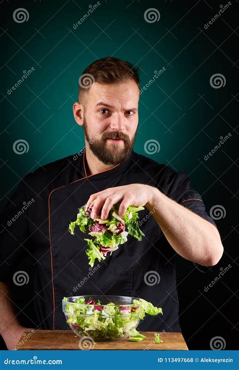 Portrait Of A Handsome Male Chef Cook Making Tasty Salad On A Blurred