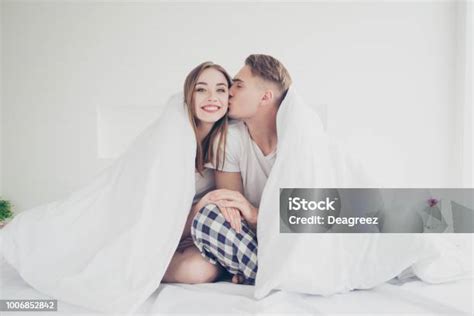 귀여운 부부는 아침에 침대에 함께 앉아 웃 고 아파트 여가에 여자를 키스 하는 남자 여자 담요에 싸여 파자마를 입고 매력적인 젊은의 초상화 2명에 대한 스톡 사진 및 기타