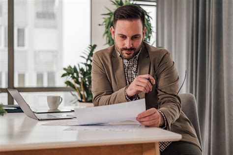 사무실 책상에서 노트북으로 작업하는 동안 문서를 분석하는 사려 깊은 사업가 재정 고문에 대한 스톡 사진 및 기타 이미지 재정
