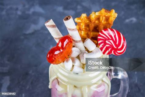 Freakshake 핑크 스무디 크림 막대 사탕 와플 마 시 멜로와 Monstershake입니다 메이슨 단지에 있는 극단적인 밀크 쉐이크 회색 어두운 콘크리트 배경입니다 0