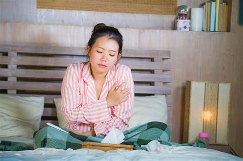 젊고 아름 다운 잠 옷에 달콤한 아시아 한국 여자 집 침실 침대 부는 그녀의 코 기침 하 고 재채기에서 온도계와 추위와 독감 복용 온도 고통에서 아픈 감기와 독감에 대한