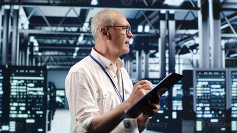 Elderly Engineer Looking Around High Tech Data Center Using Clipboard To Crosscheck Disaster