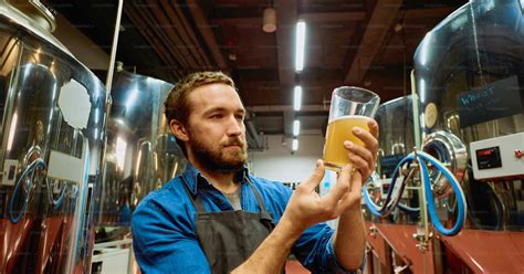 맥주 한 잔을 들고 카메라 앞에 서서 준비 후 시각적 특성을 평가하는 젊은 수염 양조자 사진 Unsplash의 공장 이미지