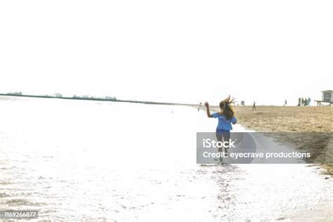 긴 갈색 물결 모양의 머리를 가진 젊은 밀레니엄 필리핀 여성은 파도와 서핑 보드를 들고 물 근처 바다의 가장자리에 모래에 실행 캘리포니아에서 물 해변을 즐기고 20 29세에