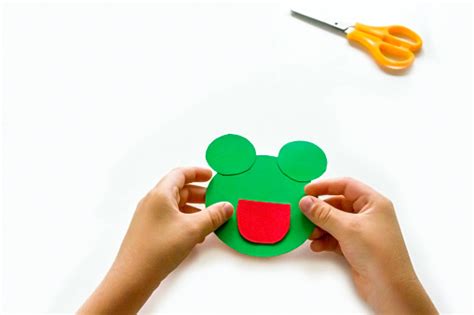 Diy와 어린이의 창의성의 개념 단계별 지시 종이에서 아플리크 개구리를 만드는 방법 5 단계 아이는 종이 원에서 개구리 얼굴을 붙입니다 선택적 초점 인공 소음 클리핑 경로