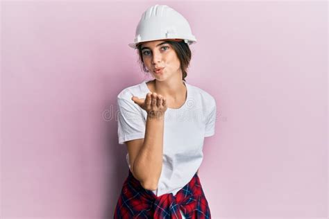 Young Caucasian Woman Wearing Hardhat Looking At The Camera Blowing A