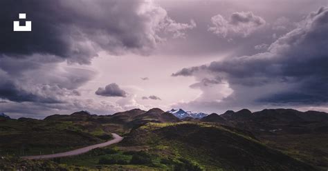 회색 구름 낀 하늘 아래 도로가 있는 녹색 산 사진 Unsplash의 무료 벽지 이미지