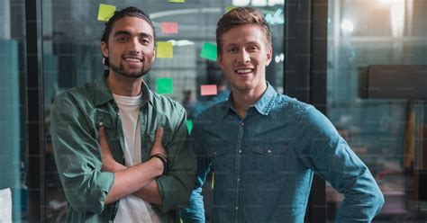 우리는 성공적인 팀입니다 자신감 넘치는 젊은 동료들의 초상화가 스티커를 붙인 유리 벽에 기대어 서서 카메라를 즐겁게 바라보고 있다 그들은 함께 일하면서 기쁨을 표현하고