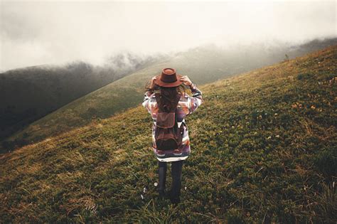 모자 산 위에 걷는 Hipster 세련 된 소녀 안개 산맥을 탐험 하는 책 가방을 가진 행복 한 젊은 여자 여행과 방 랑 벽 개념입니다 놀라운 대기 순간 개념에 대한 스톡