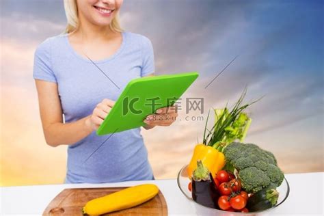 健康饮食、食品、技术和人的概念 关闭微笑的年轻女子与 Tablet Pc 计算机和一碗蔬菜在天空背景。高清摄影大图 千库网