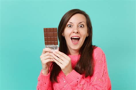 흥분된 젊은 여성 니트 핑크 스웨터 입 유지에 열고 찾고 놀 손에 초콜릿 바 블루 배경 스튜디오 초상화에 고립 사람들의 라이프