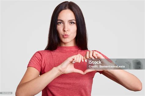 아름 다운 갈색 머리 여성 캐주얼 빨간 T셔츠에 게 양손으로 하트 기호 둥근 입술을 유지 건강 한 피부 흰색 배경 위에 절연 모두에 게 사랑을 표현 신체 언어 T 셔츠에