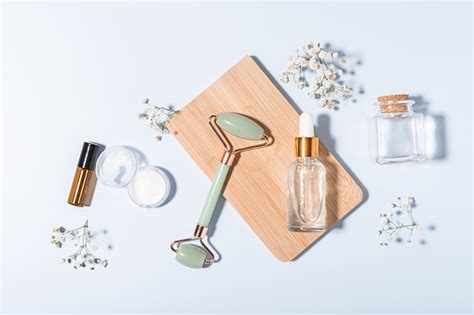 녹색 옥 돌 롤러 마사지기 Guasha와 흰색 꽃과 밝은 파란색 배경에 나무 스탠드에 유리 화장품 병 얼굴 치료와 스파 천연 유기농 미용 제품 마사지 오일 0명에 대한 스톡