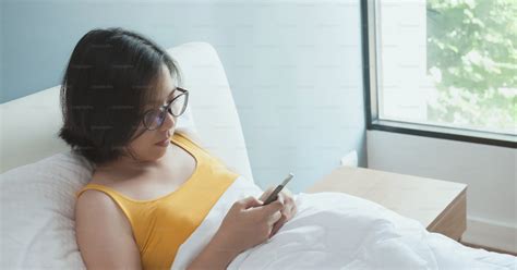 침대에 스마트폰을 들고 누워 있는 젊은 아시아 여성의 편안한 분위기 사진 Unsplash의 문자 메시지 이미지