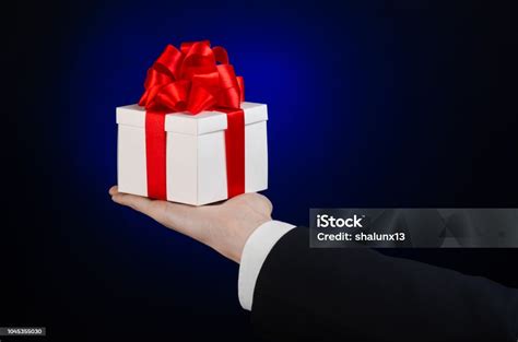 축 하와 선물의 테마 절연 스튜디오에 진한 파란색 배경에 독점적인 선물 레드 리본 아름 다운 흰 상자에 싸여 비싼 선물 들고 검은 양복에 남자 기념일에 대한 스톡 사진 및
