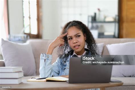 유익한 웹 사이트를 탐색하기 위해 Wifi에 연결된 대학 과정 작업의 문제로 두통을 느끼는 지친 여학생 노트북에서 전자 학습에 지친 불행한 어두운 피부 여성 계획에 대한