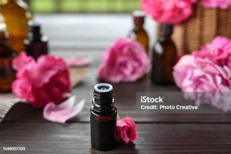 나무 테이블에 아로마 오일이 있는 구성 클로즈업 나무 테이블에 장미 에센셜 아로마 오일이 있는 병 꽃 에센셜 오일 약초 측면도 선택적 초점 건강관리와 의술에 대한 스톡 사진