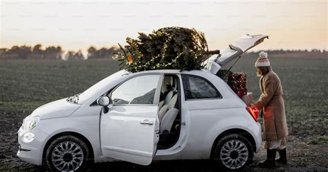 황혼에 자연의 옥상에 크리스마스 트리와 함께 차에 선물을 포장하는 여자 새해 연휴 준비 크리스마스 분위기에 대한 아이디어 모피 코트와 모자를 쓴 여자 사진