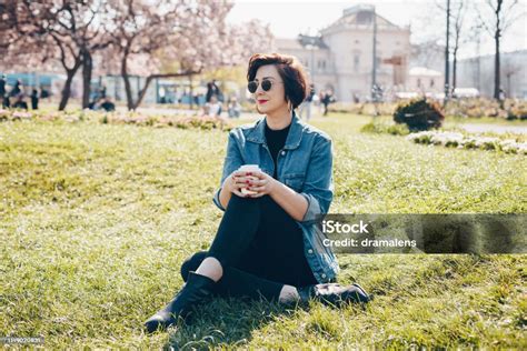 공원에 앉아 휴식을 취하는 아름 다운 여자 가 서 커피를 마시는 매력적인 갈색 머리의 초상화 따뜻한 봄 날 야외에서 즐기는 현대 소식통 세련 된 소녀 스트리트 스타일