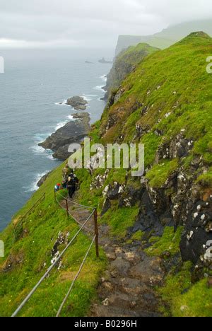 Hike To The Lighthouse On Mykines Faroe Islands A Tourist In A Red Jacket Walks Along The
