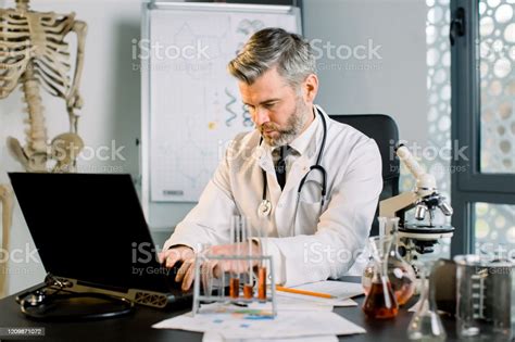 잘 생긴 수염 남성 수석 전문 과학자 테이블에 앉아 노트북에 작업 테스트 튜브 유리 플라스크와 현대 실험실에서 테이블에 현미경 의학 화학 생물학 Stem 주제에 대한 스톡