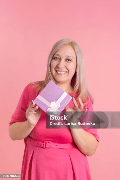 손에 선물 상자를 들고 있는 중년 여성이 분홍색 드레스를 입고 분홍색 배경에 서 있다 세로 사진 35 39세에 대한 스톡 사진