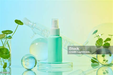 유리 받침대 위에 서 있는 화장품 스프레이 병의 정면 아시아 페니워트 식물로 둘러싸인 투명한 유리 구체 파란색 배경에 표시된 병풀 비커가 있는 코일 콘덴서 0명에 대한 스톡