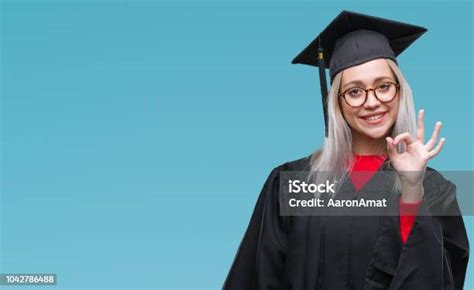 젊은 금발 여자 격리 된 배경 손과 손가락으로 Ok 사인을 하 고 긍정적인 미소를 통해 대학원 유니폼을 입고 성공적인 식입니다 교육에 대한 스톡 사진 및 기타 이미지