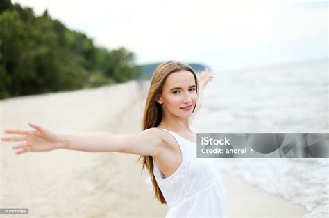 두 손을 벌리고 서 있는 바다 해변에서 자유로운 행복의 행복을 누리고 있는 행복한 미소 짓는 여자 흰색 여름 드레스를 입은 다문화 여성 모델의 초상화는 야외 휴가 동안